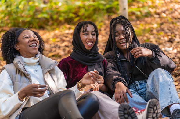 Multi-ethnic friends laughing sitting on a park Stock Photo by Unai82
