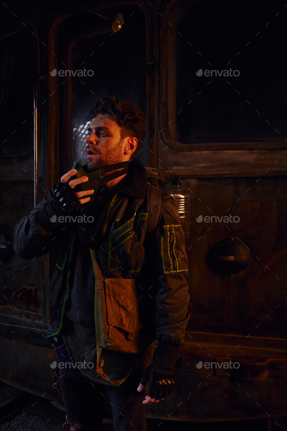 man in worn outfit holding gas mask and looking away in abandoned ...