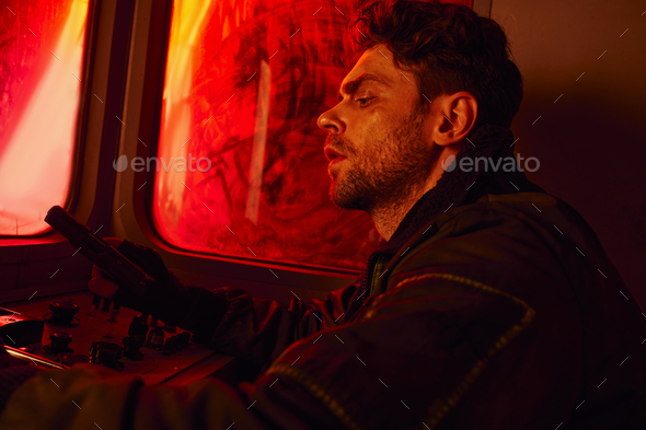unshaven man with gun near dashboard of subway carriage in red light ...