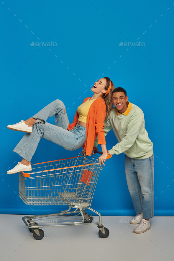 cheerful african american man riding shopping cart with girlfriend ...