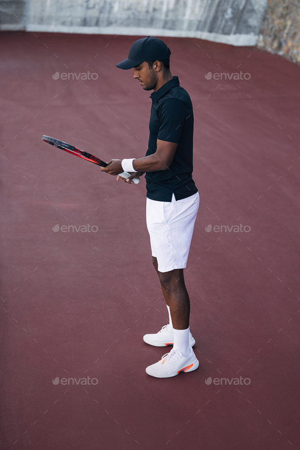 Side view of a male tennis player in sportswear adjusting his racket ...