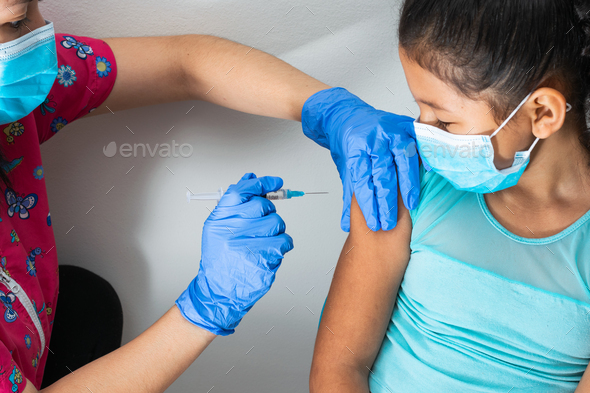 children's nurse injecting arm of little brown girl, girl watching ...