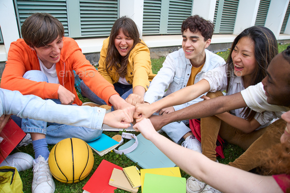 Diverse young friends gathered in circle sitting on campus excited fist ...