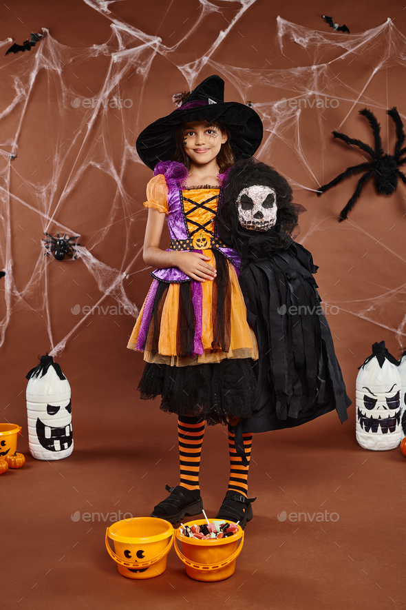 cheerful girl in witch hat with cobweb makeup holding spooky toy on ...