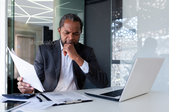 Serious thinking businessman behind paper work inside office, senior ...