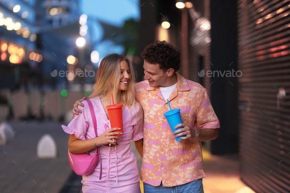 Gen Z couple in pink outfits leaving the cinema with drinks in hand ...
