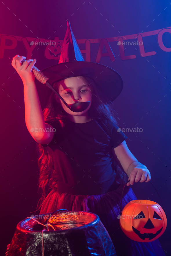 Child girl witch cooking a potion in the cauldron at halloween holidays ...