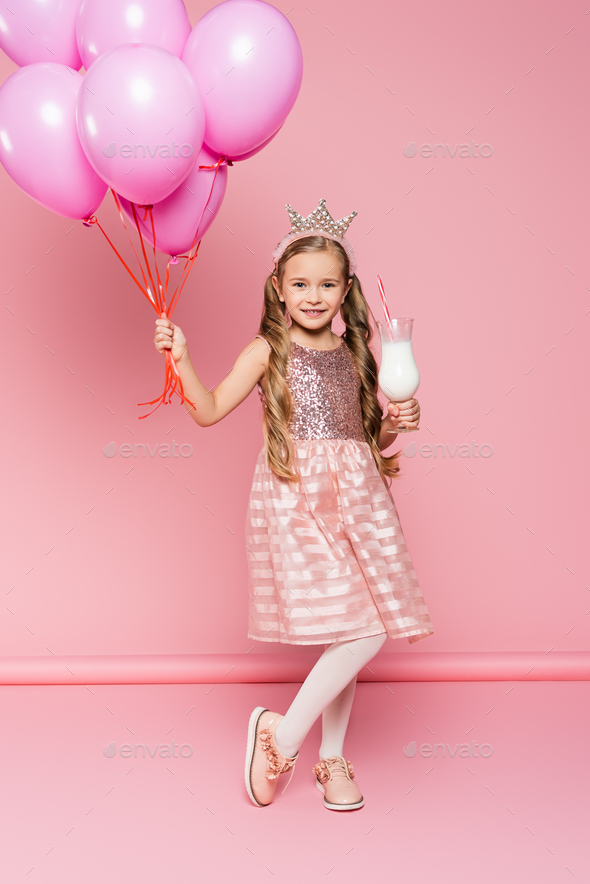 full length of cheerful little girl in dress and crown holding glass ...