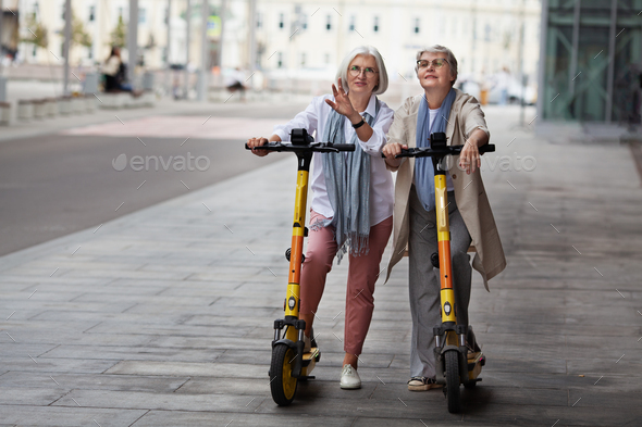 Senior women with gray hair enjoying ride together on electric scooters ...