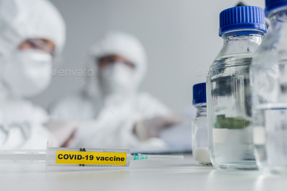 Syringe with covid-19 vaccine lettering near scientists in laboratory ...
