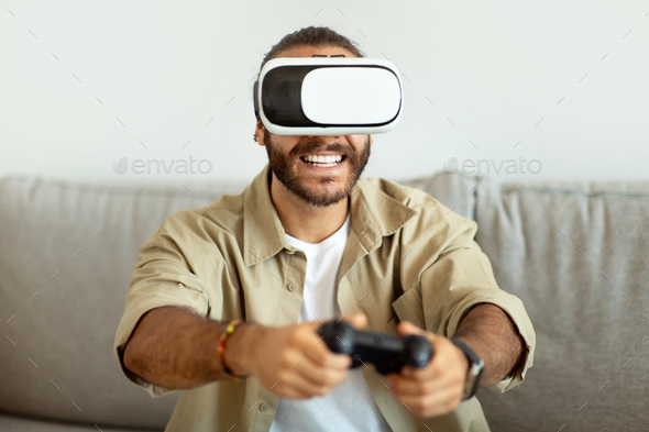 Smiling young guy using VR goggles and console at home Stock Photo by ...