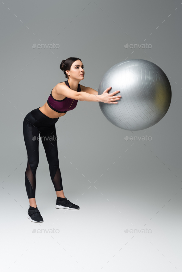 sportswoman doing forward bend exercise with fitness ball on grey ...