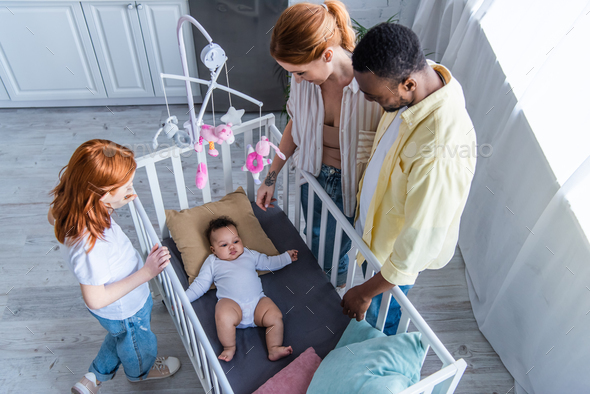 overhead view of multiethnic family looking at infant girl lying in ...