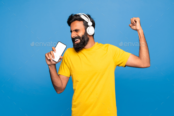 Happy indian man in wireless headphones singing at smartphone with ...