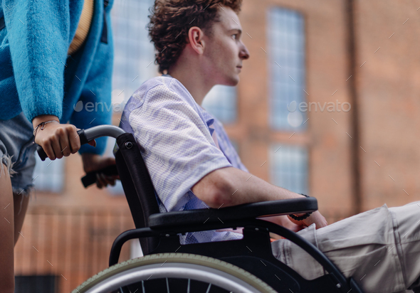 Sad gen Z boy in a wheelchair with friends in the city. Stock Photo by ...