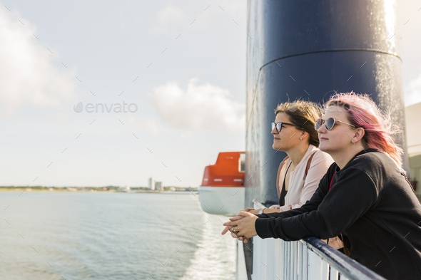 Two women leaning on railing on ship deck Stock Photo by astrakanimages