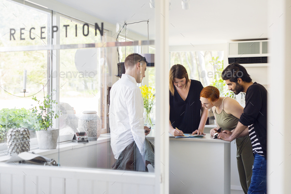 Guests talking with hotel receptionist Stock Photo by astrakanimages