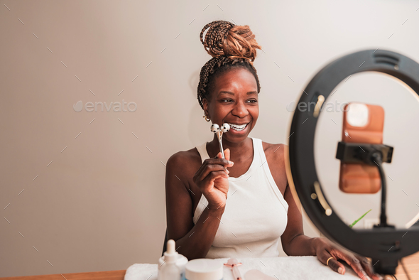 Smiling influencer filming tutorial with facial magnet roller in front ...