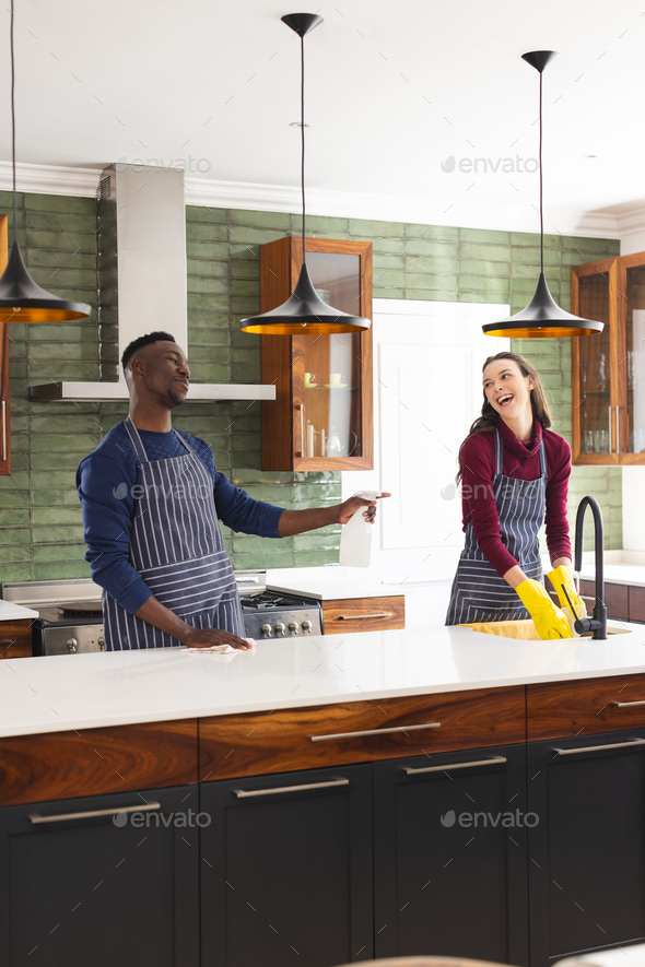 Happy diverse couple cleaning countertop and doing dishes in kitchen at ...