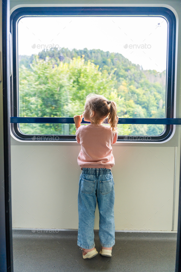 Little girl looking out train window outside, while it moving ...