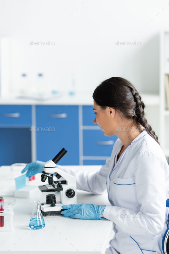 Side view of scientist working in laboratory with microscope and flask ...