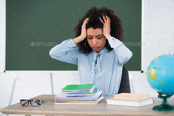 Tired african american teacher having headache near stationery and ...