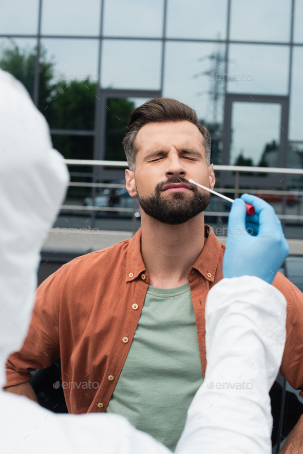 Man with closed eyes standing near medical worker with pcr test ...