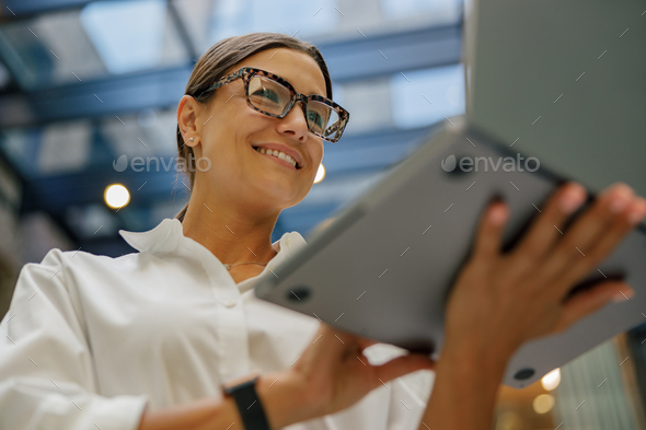Stylish business woman in eyeglasses working on laptop standing on ...