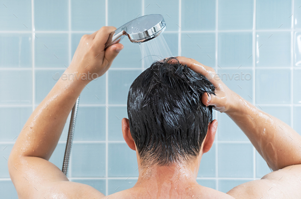 Man washing his hair in the shower against background of blue tiles ...