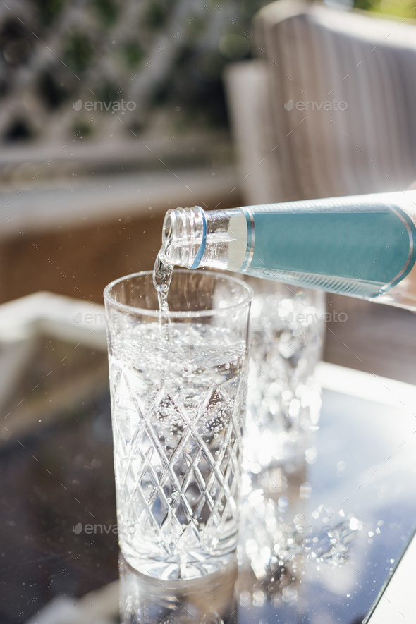Pouring sparkling water from the bottle into glass. Water drink pouring into glass, garden Stock ...