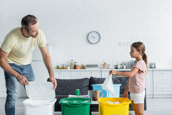Father and daughter sorting garbage in trash cans with recycle sign in ...