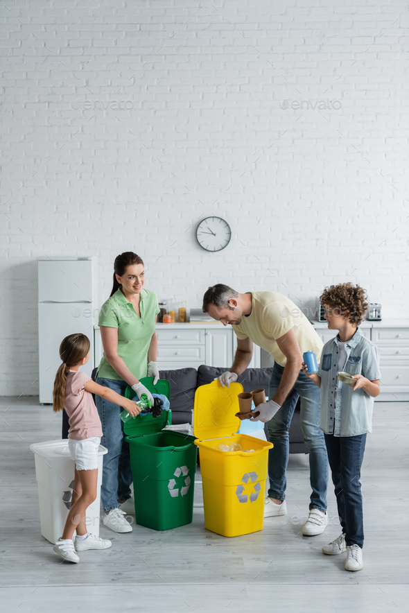 Cheerful family sorting trash in cans with recycle emblem at home Stock ...