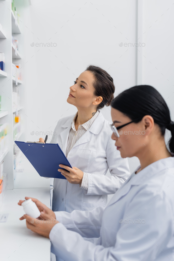pharmacist in white coat holding clipboard while checking medication ...