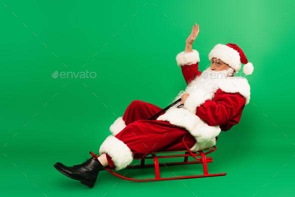 Santa claus waving hand while sitting on sleigh on green background ...