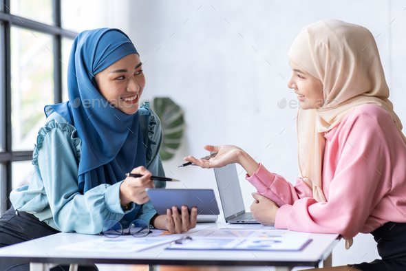 Two Young muslim business women point to graphs and charts to analyze ...