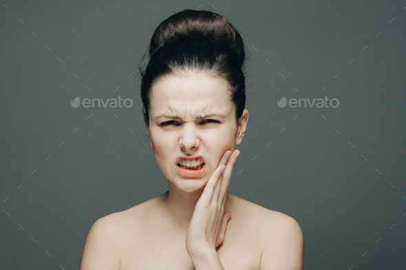 brunette displeased expression holding hand on face gray background ...