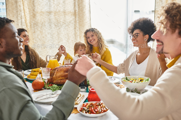 cheerful multiracial friends and family holding hands and praying ...