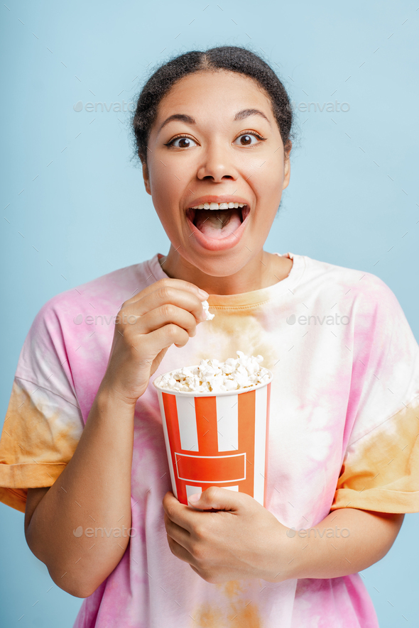 Excited African American woman holding bucket with popcorn, eating ...