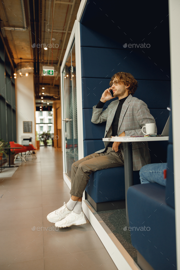Male boss talking phone with client while sitting in coworking space ...
