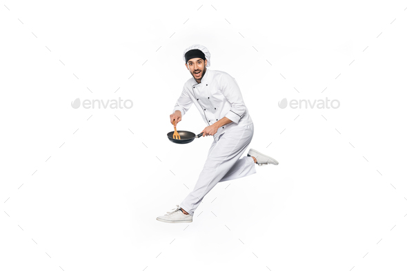 smiling chef in hat and uniform jumping and holding frying pan with ...