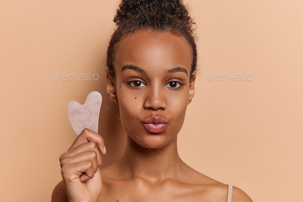 Photo of dark skinned lovely woman holds gua sha stone for face ...