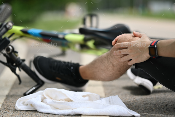 Man with injured knee sitting near bicycle outdoors, falling down from ...