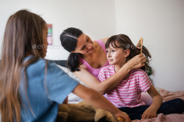 Mother with two daughters on a bed in the bedroom. Mother combs ...