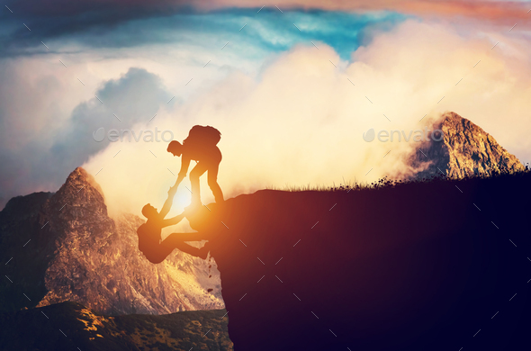 Man giving his hand to help his friend climb up the mountain Stock ...