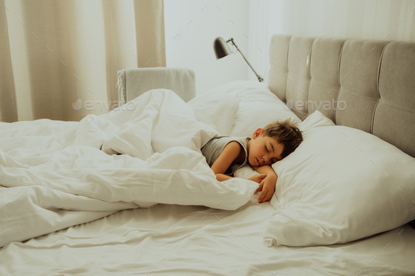 Calm little child sleeping well in comfortable bed. Boy in light cozy ...