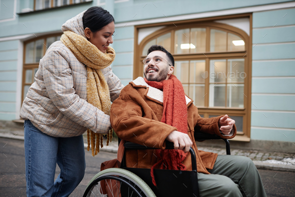 Smiling young woman assisting partner with disability in city streets ...