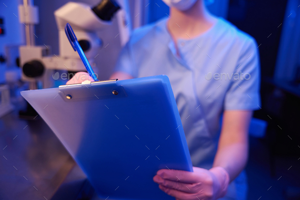 Lab researcher recording results after microscopic examination of cell ...