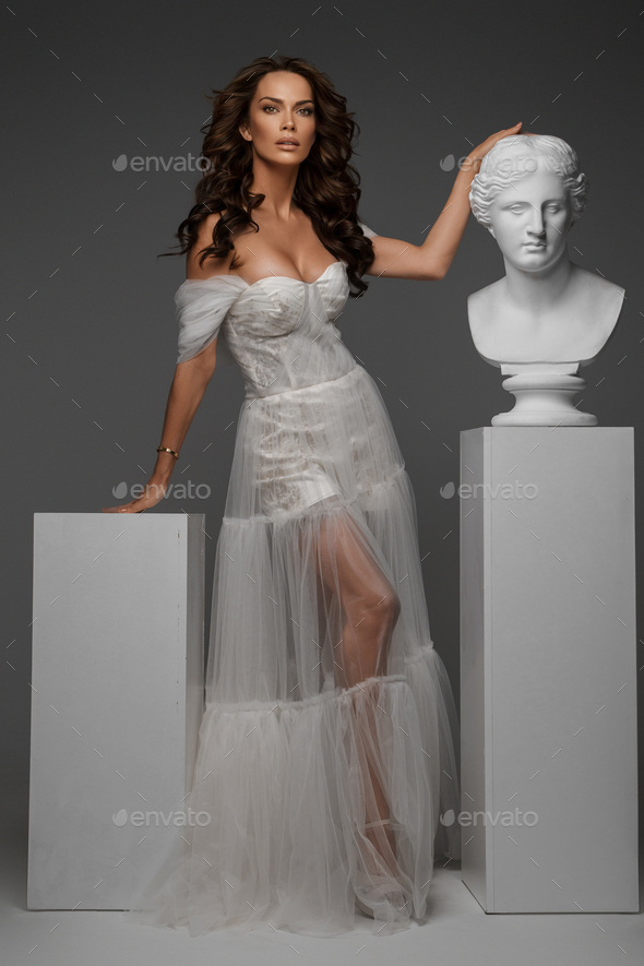 Stunning model in a luxurious white dress poses with ancient Greek ...