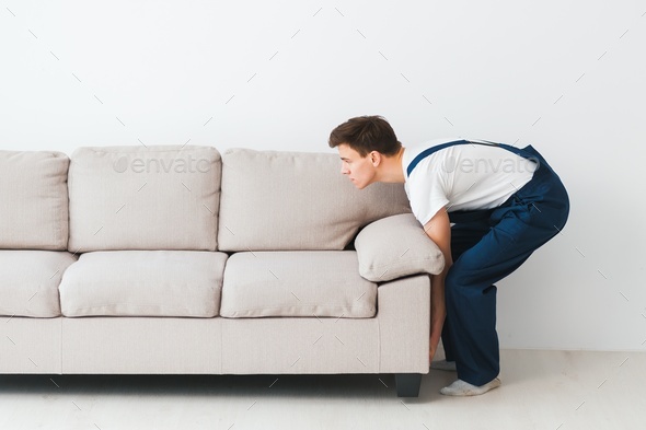 Loader moves sofa, couch. worker in overalls lifts up sofa, white ...