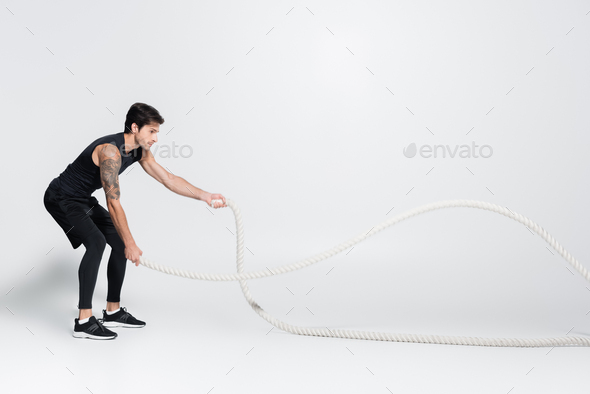 Side view of athletic sportsman holding battle ropes during cross ...